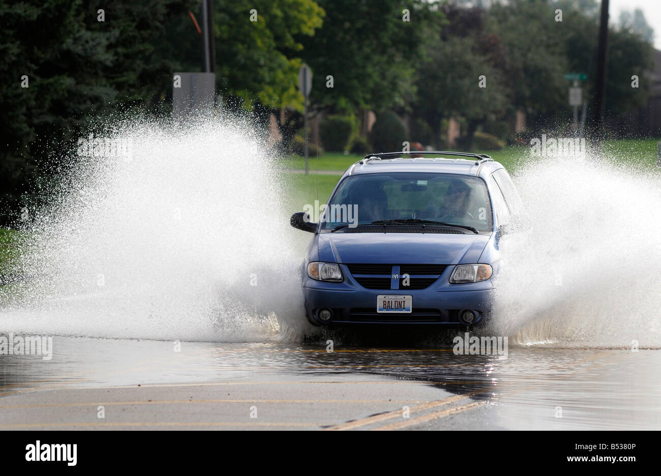 A mini van drives through standing water on a suburban street Stock ...
