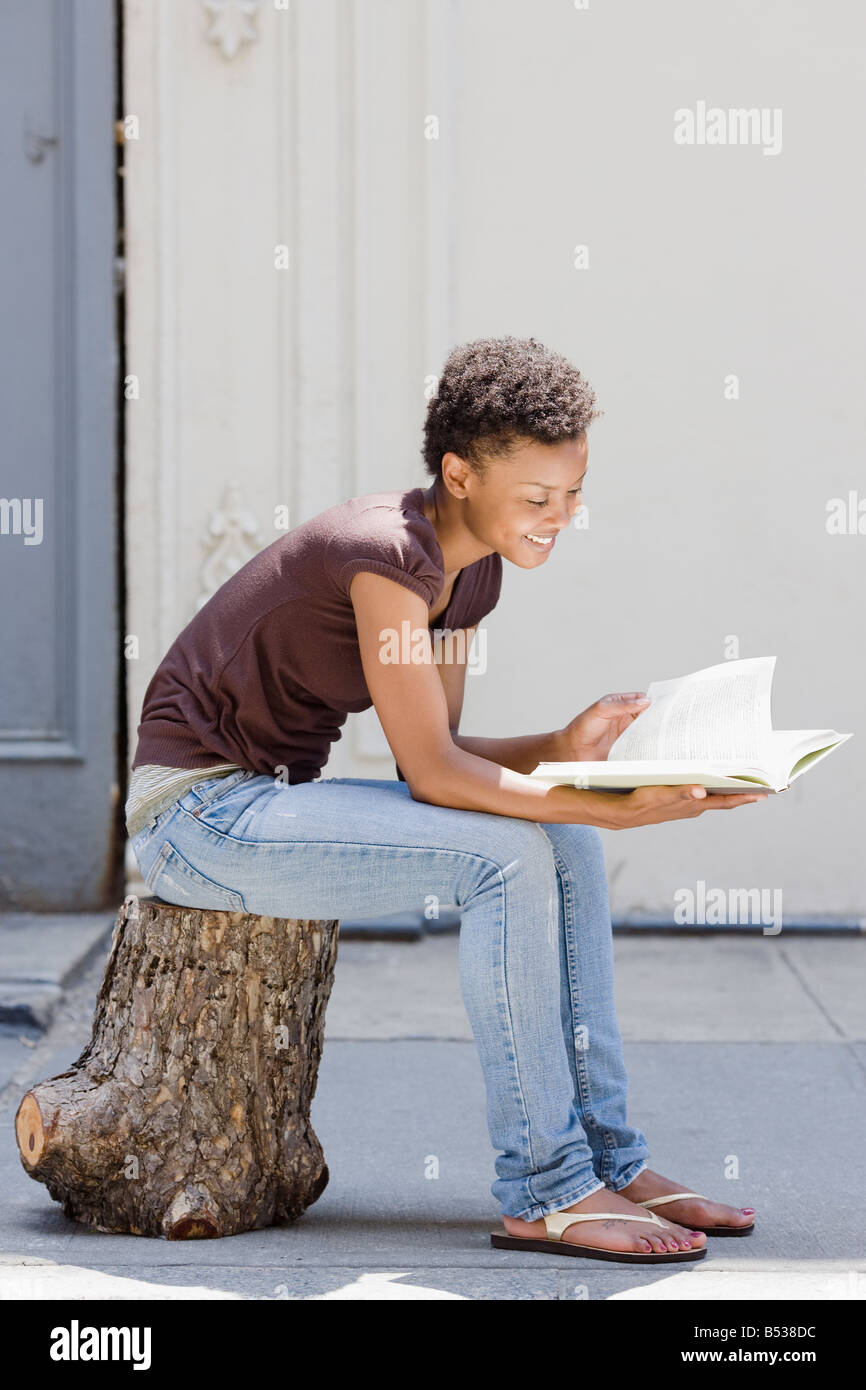 African woman sitting on tree stump and reading Stock Photo - Alamy
