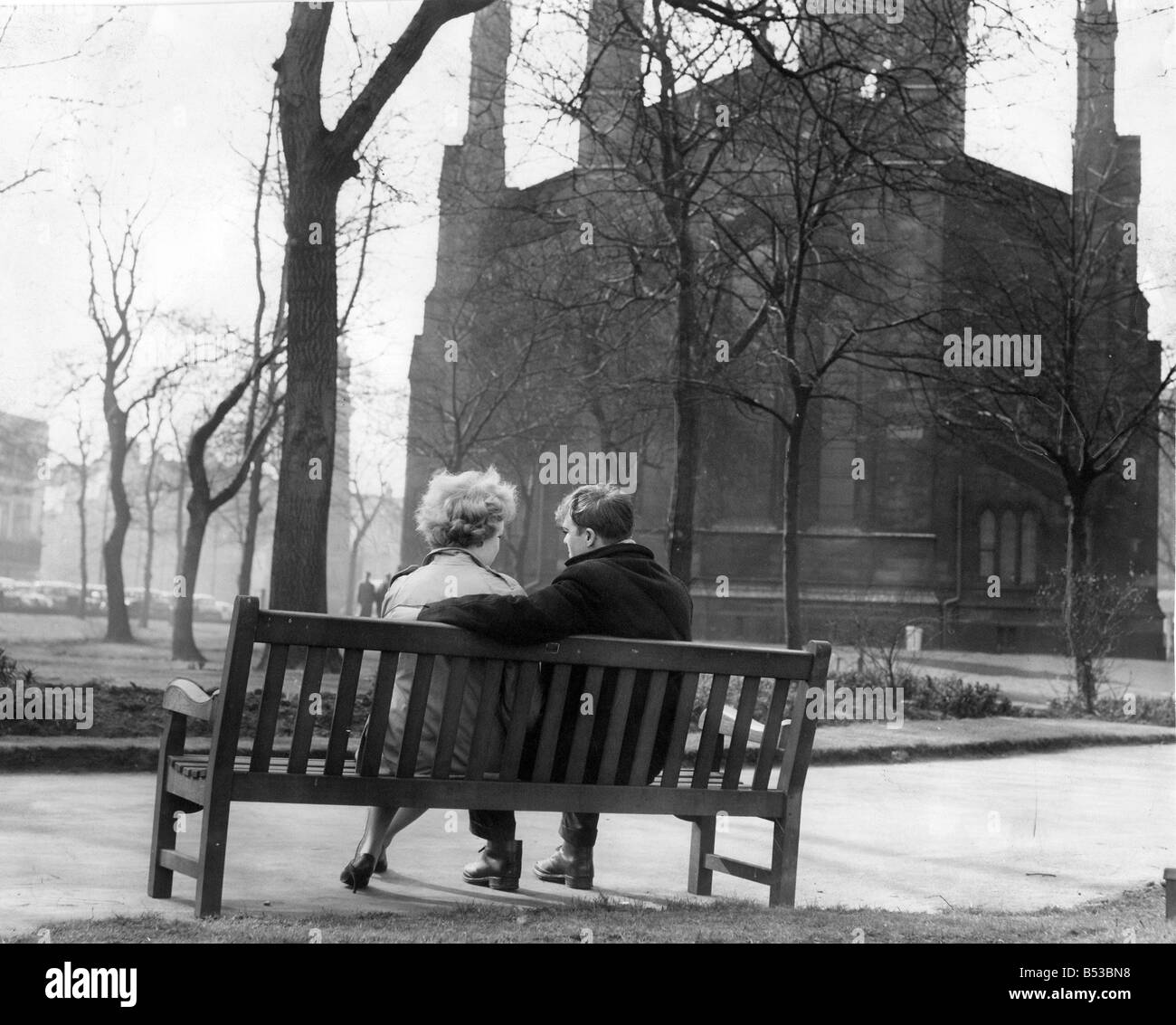 A young couple enjoy a cuddle on a park bench Stock Photo - Alamy