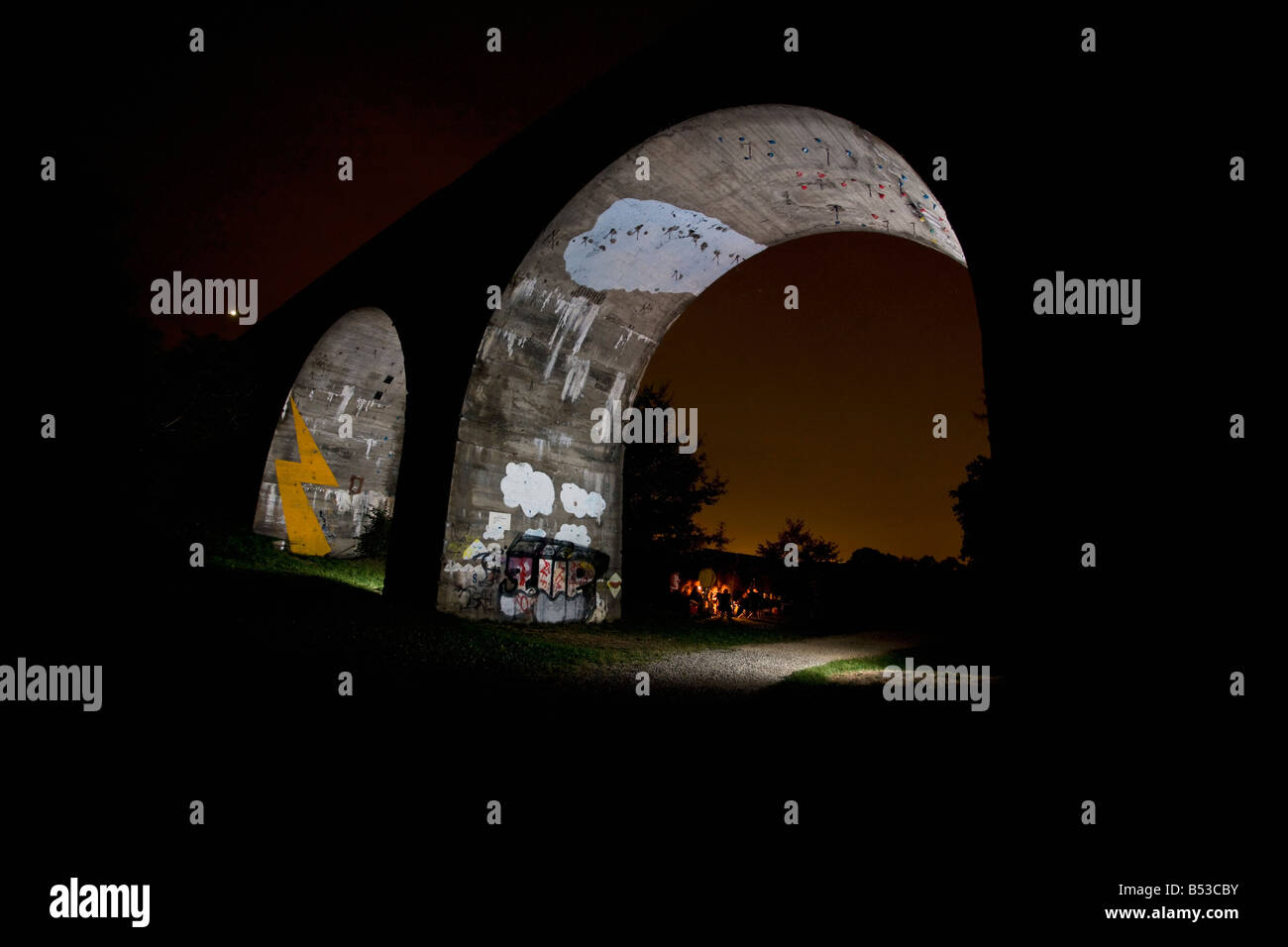 Younger people sitting around bonfire at night near painted bridge ...