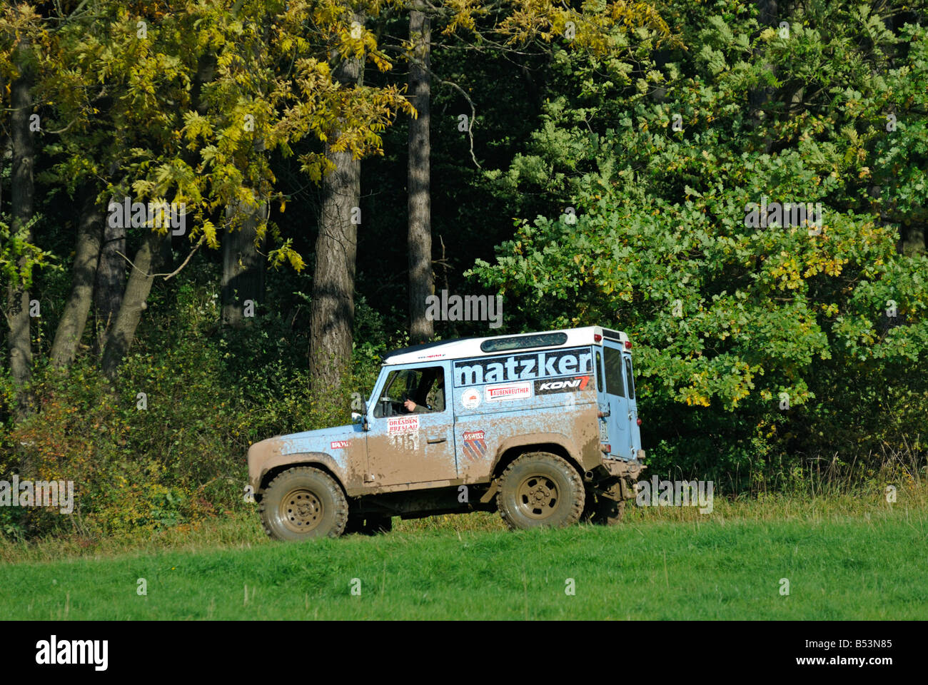 Muddy light blue Land Rover Defender 90 driving along a forest track in ...