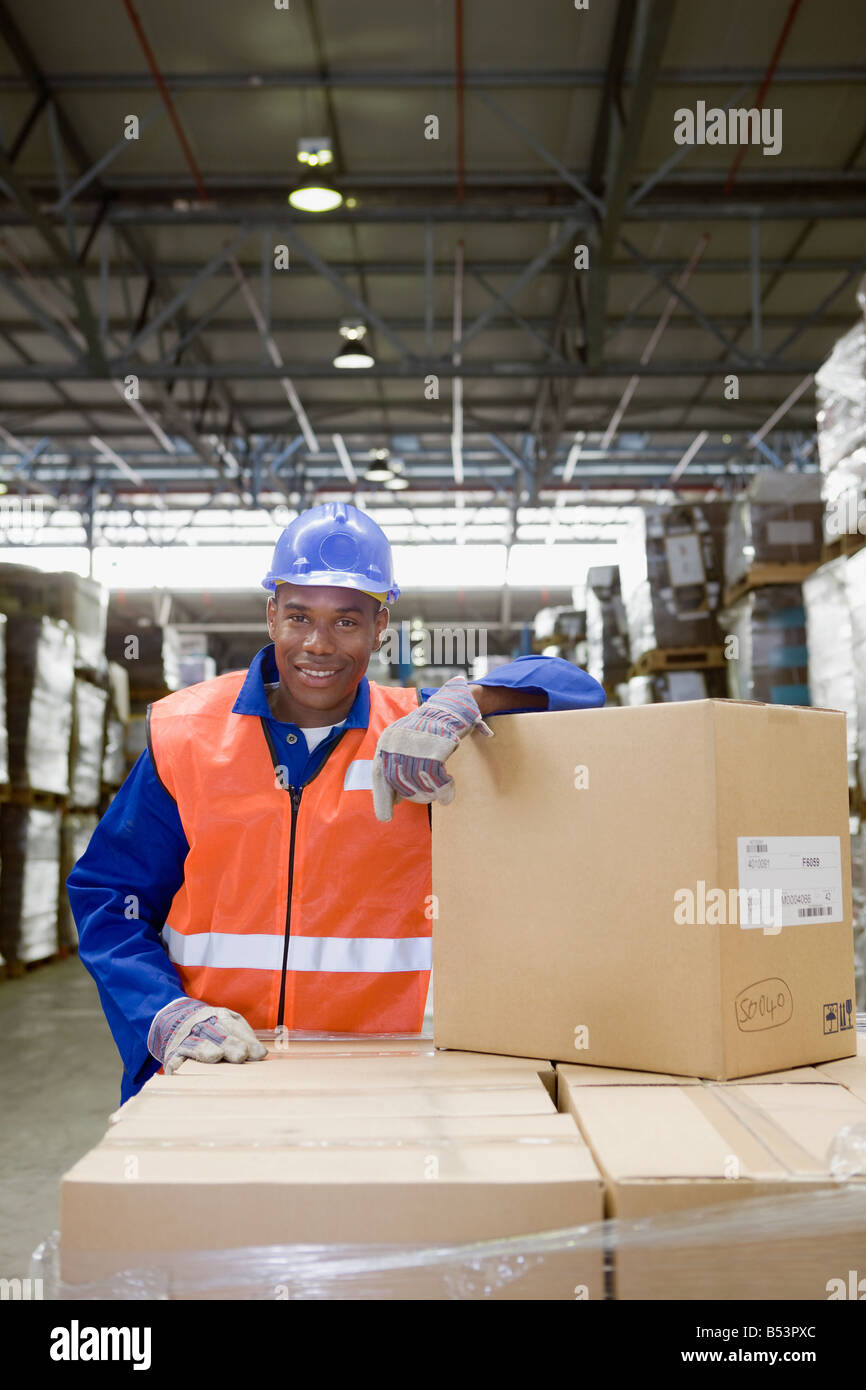 African worker leaning on boxes in warehouse Stock Photo - Alamy