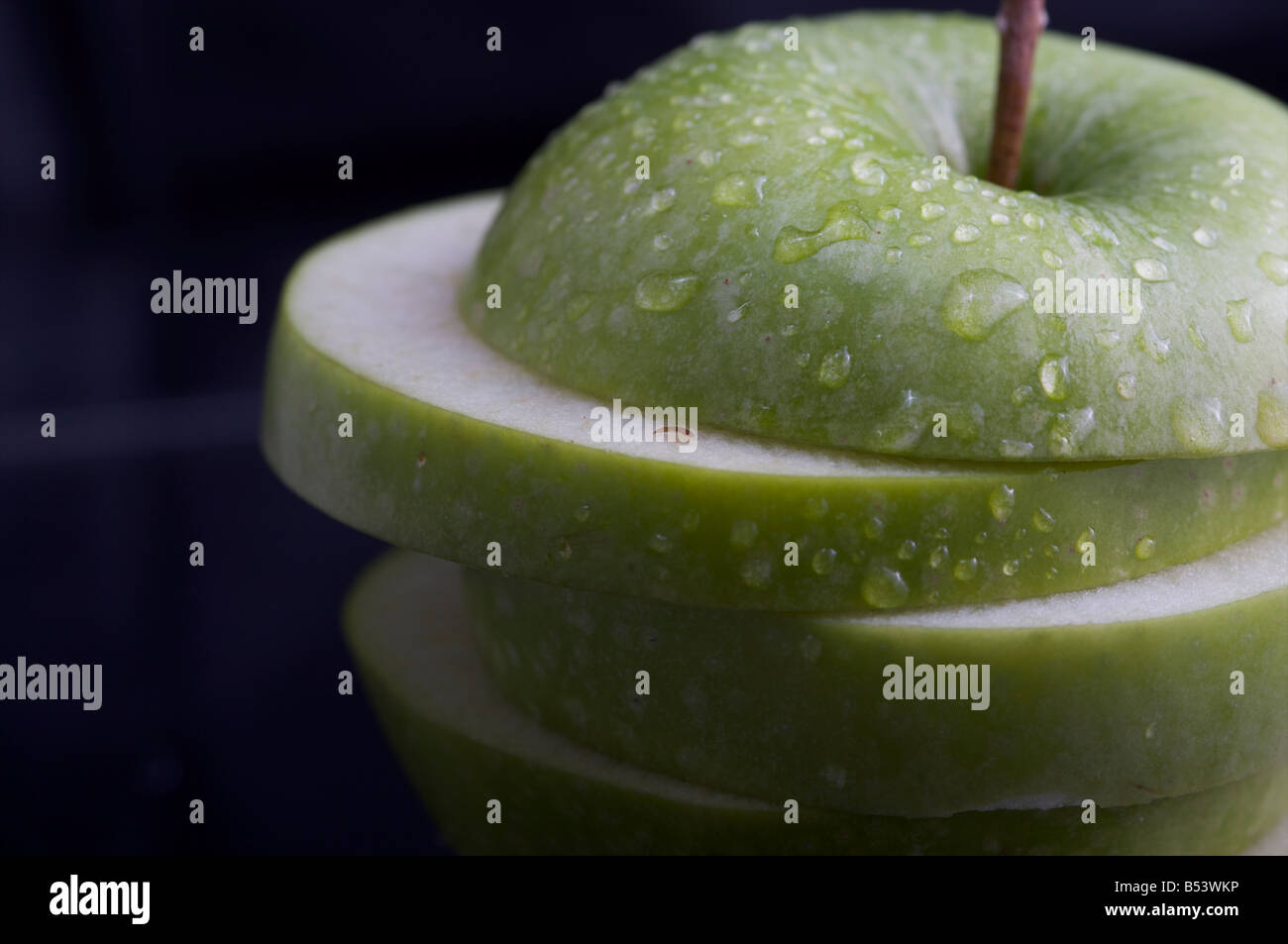 Picture Shows a green apple cut in to slices and stacked ontop of each ...