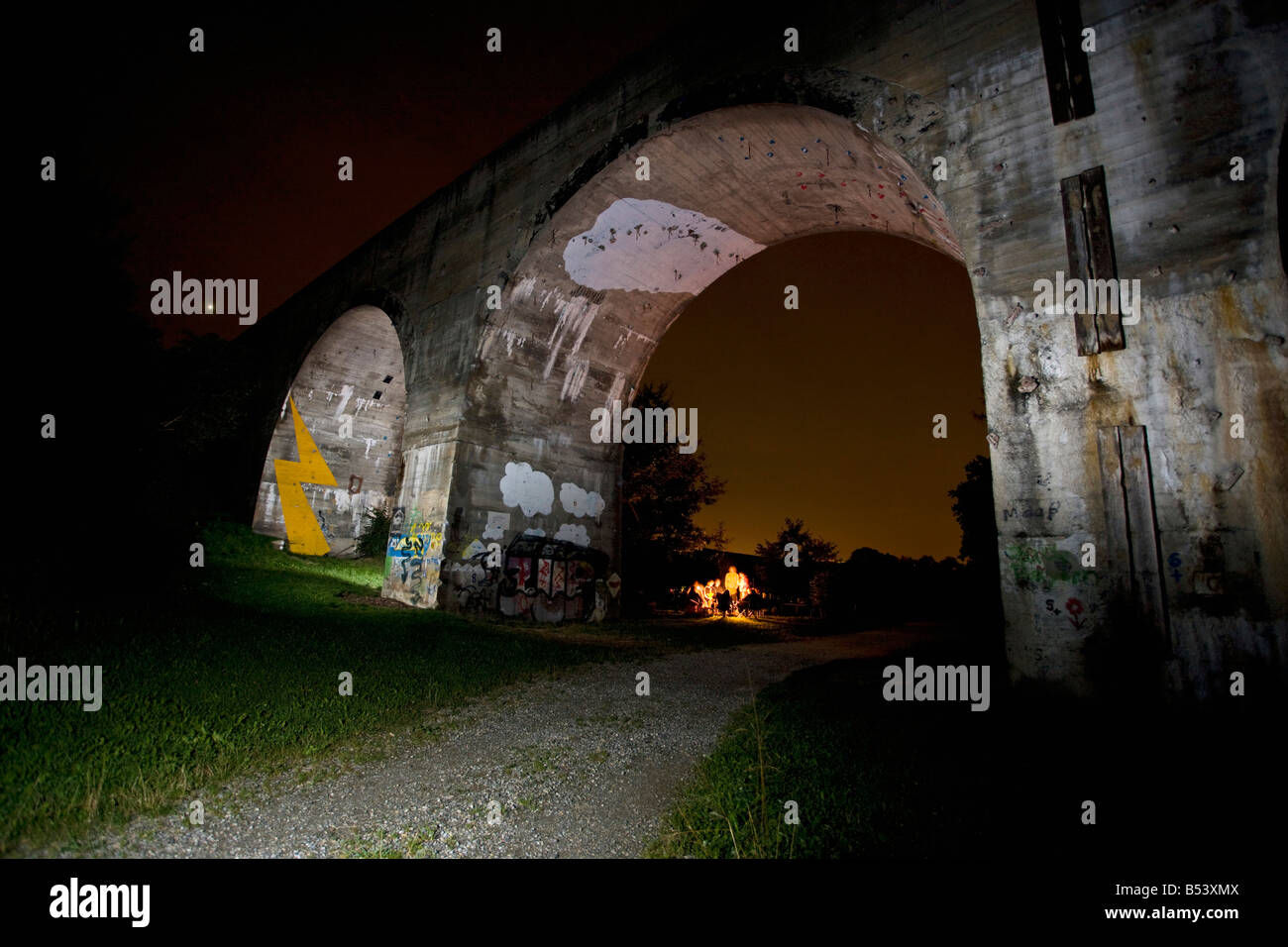 Younger people sitting around bonfire at night near painted bridge ...