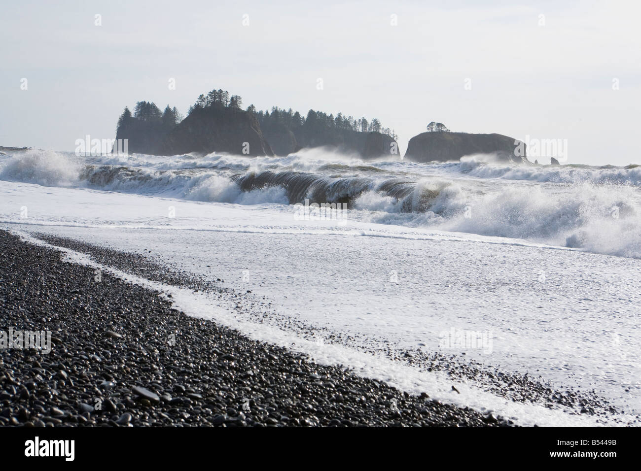 Waves crashing on a stoney beach with sea stacks out beyond the surf at ...