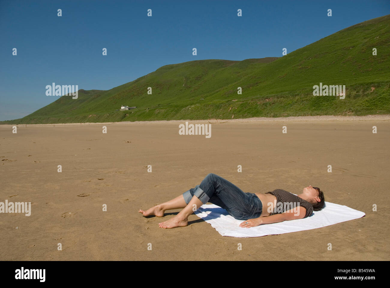 Young woman sun bathing on a towel on the beach, Rhossili Beach, Gower ...