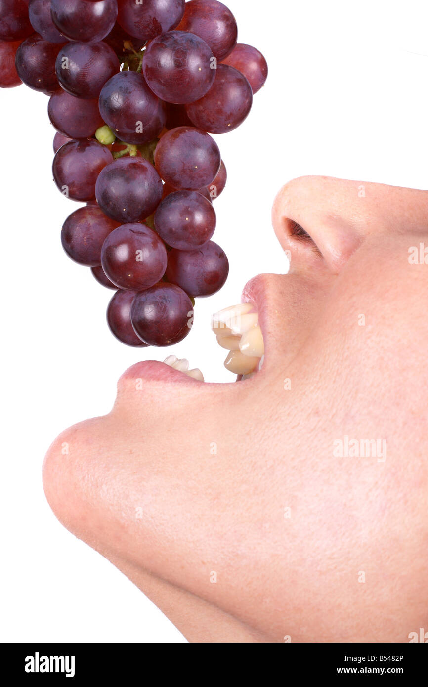 Beautiful young woman eating red grapes, isolated on white background ...