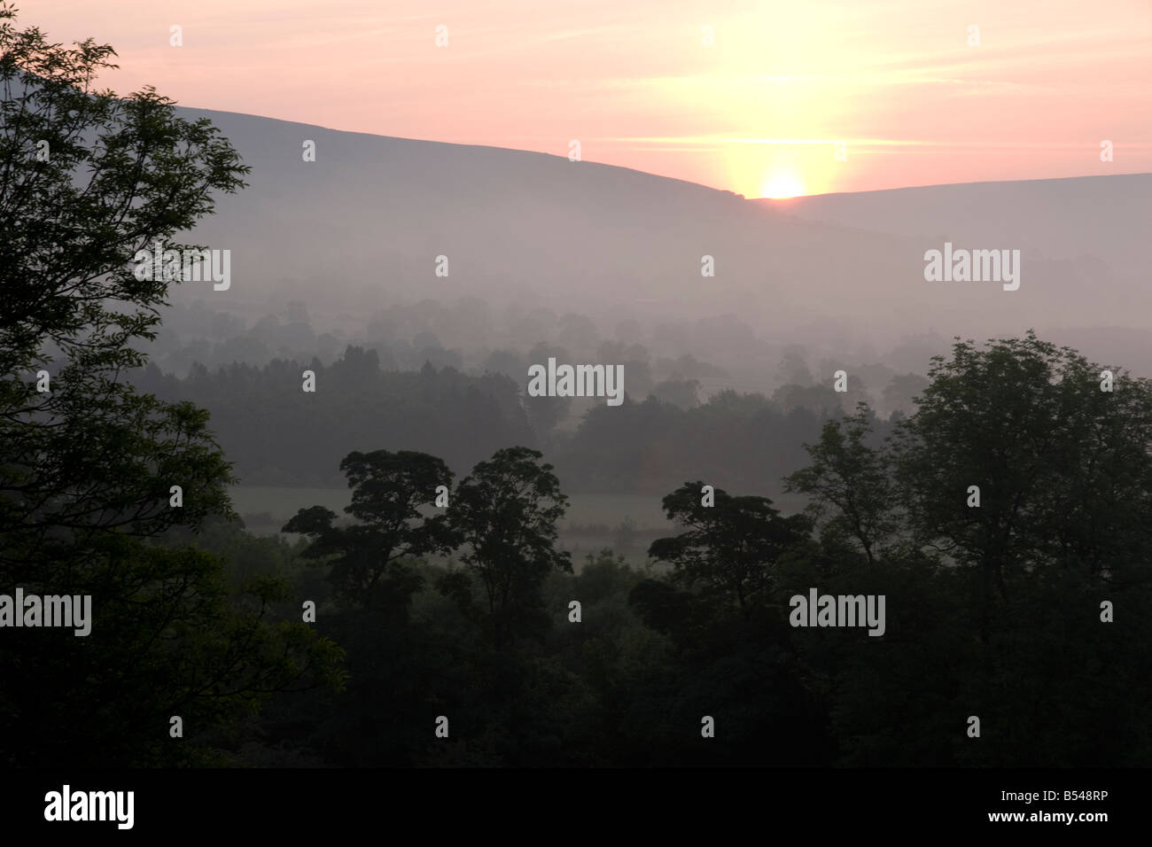 dawn over the castleton valley with trees and mist in the landscape ...