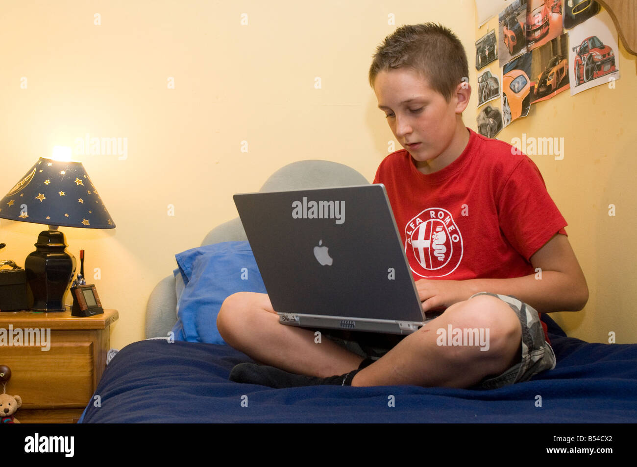Tired looking teenage boy using a laptop computer in his bedroom at ...