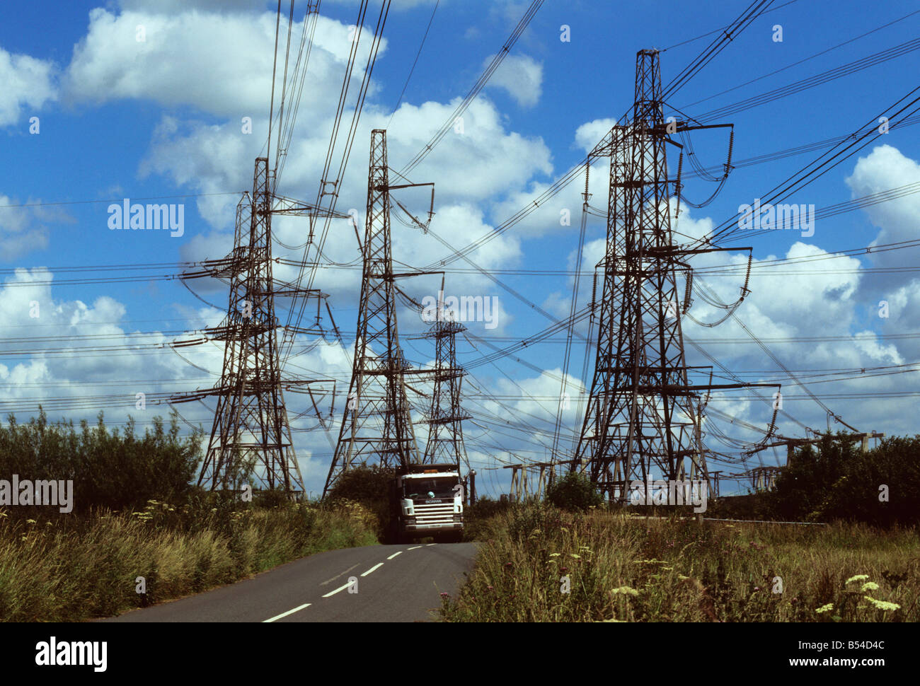 lorry travelling on country road passing giant electricity pylons at ...