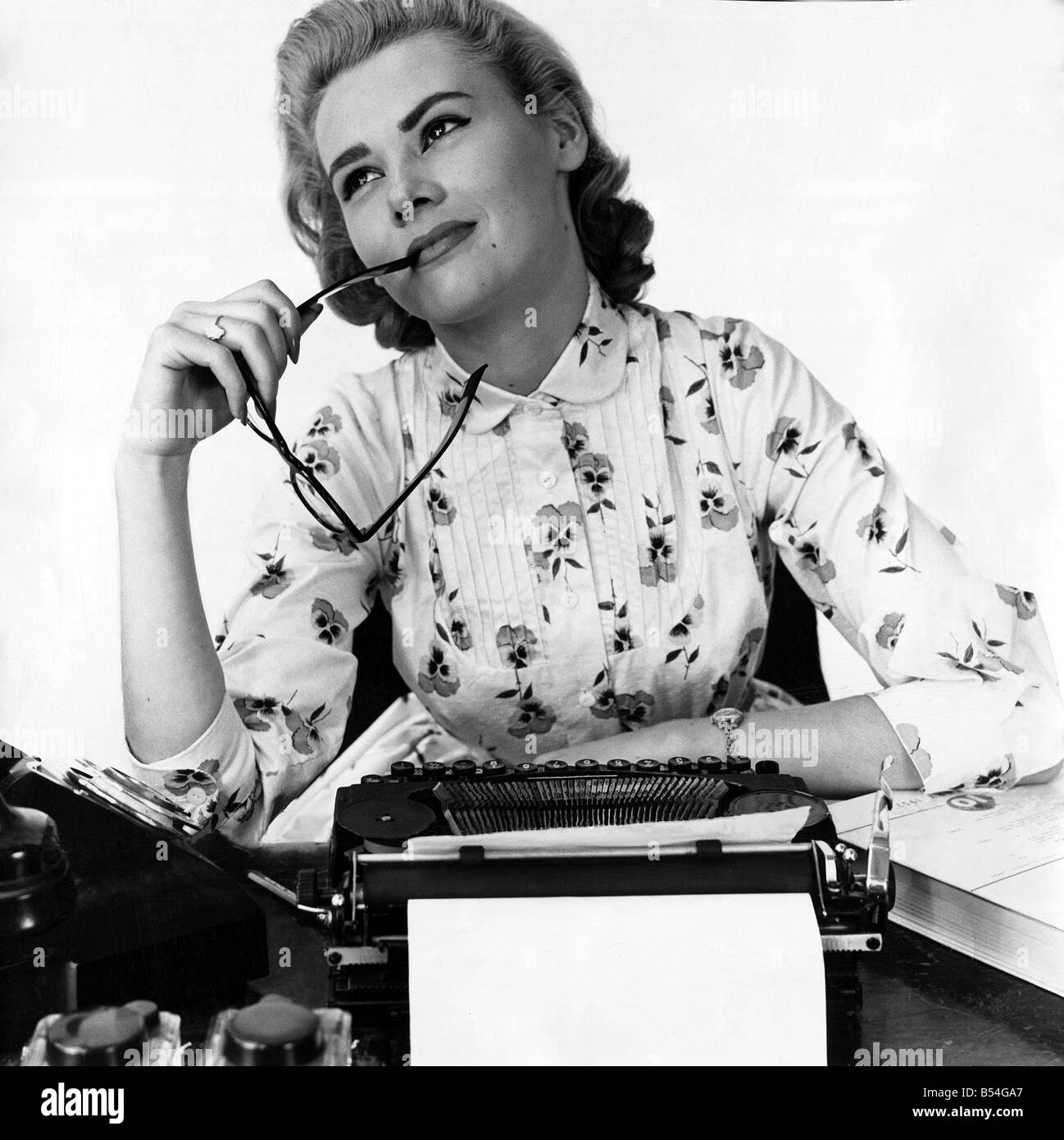 Secretary at typewriter chewing the end of her glasses daydreaming ...