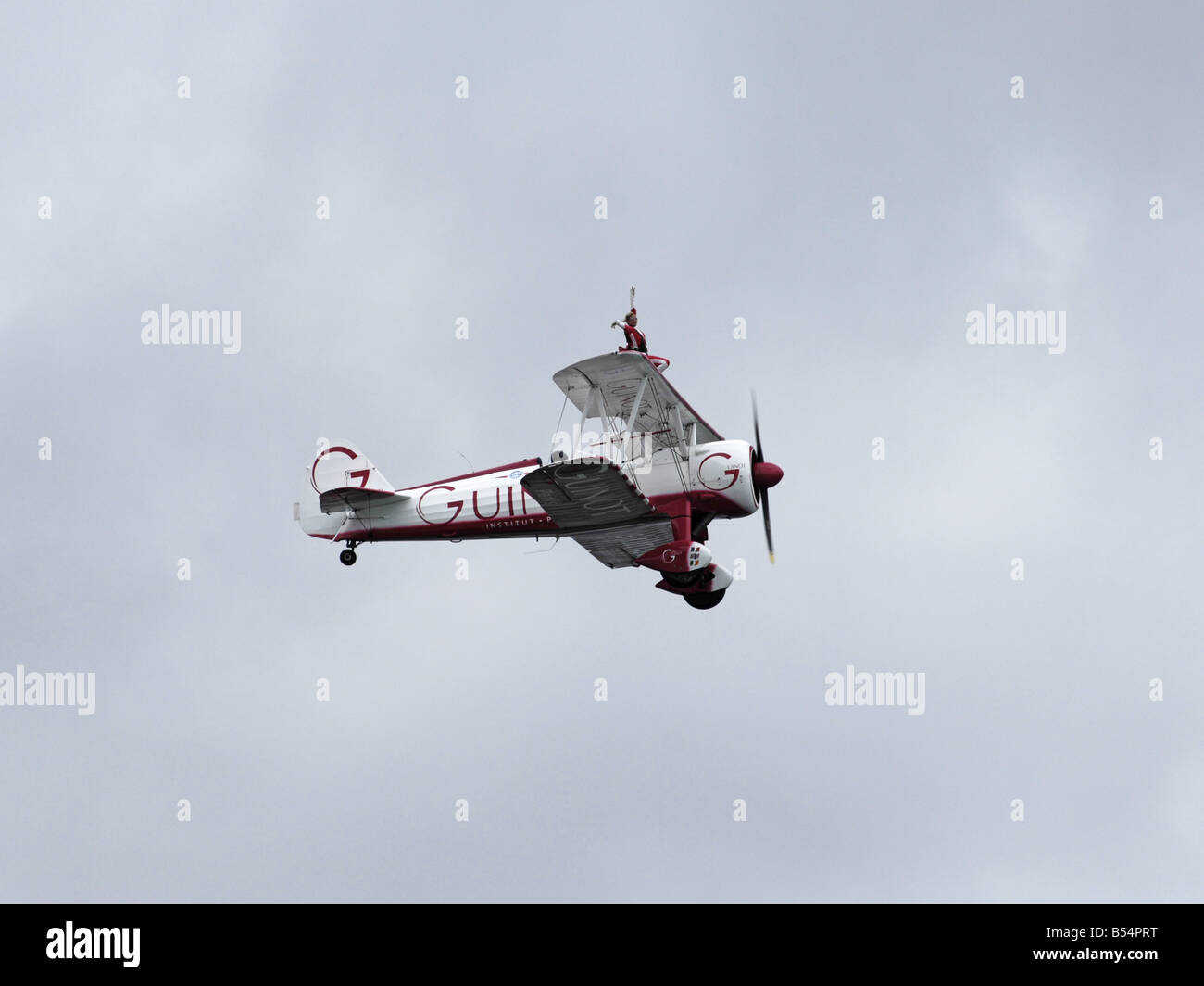 Stunt flying bi-plane with a female wing walker standing on the top ...