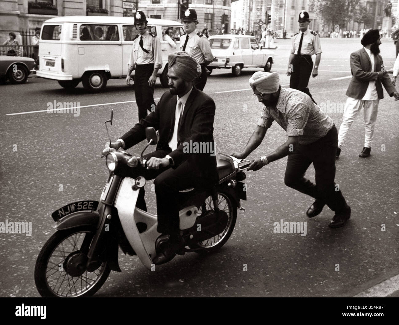 A Sikh man riding a motorcycle wearing a turban pushes by a fellow sikh ...