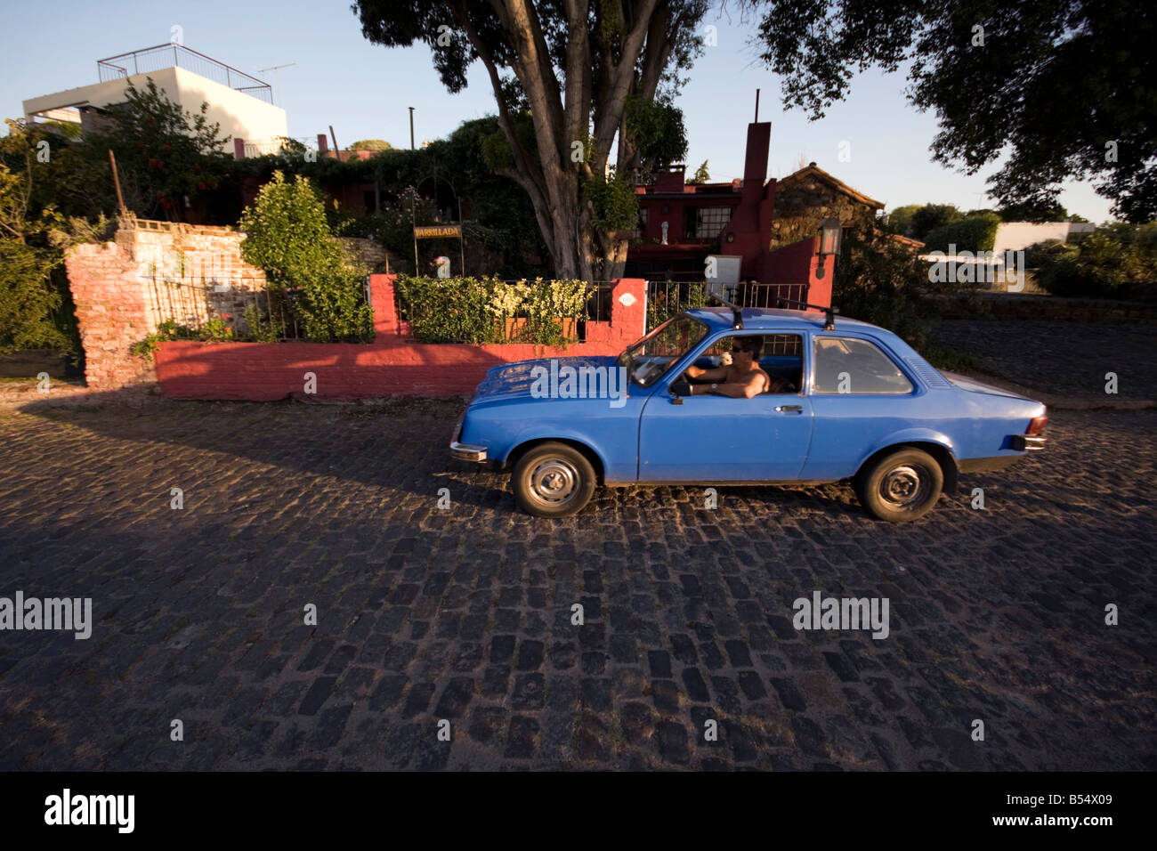 A man driving a blue car along a cobbled street in Colonia del ...