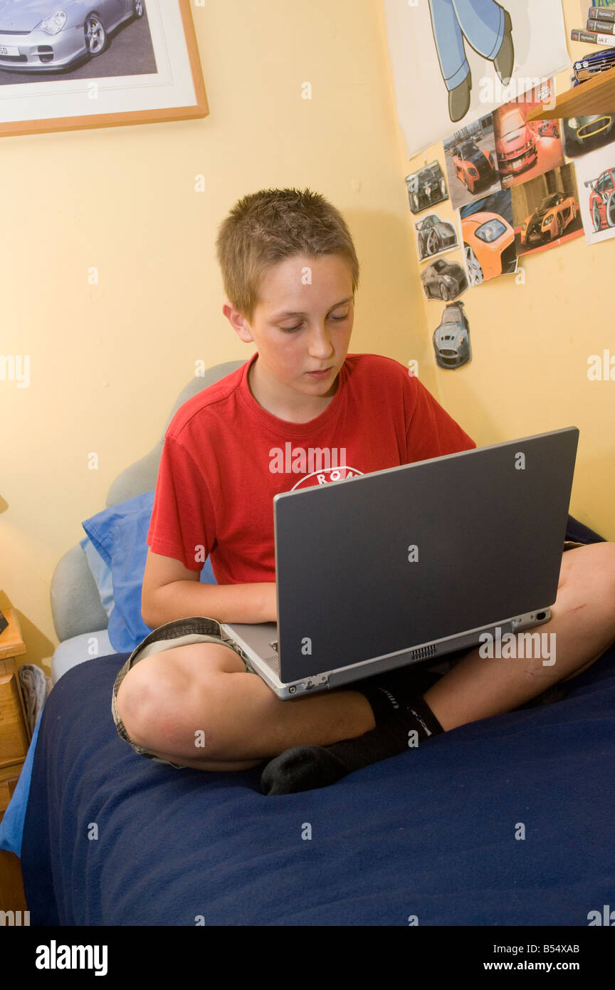 Tired looking teenage boy using a laptop computer in his bedroom at ...