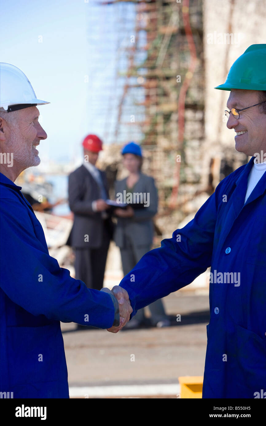 Two construction engineers shaking hands with colleagues standing ...