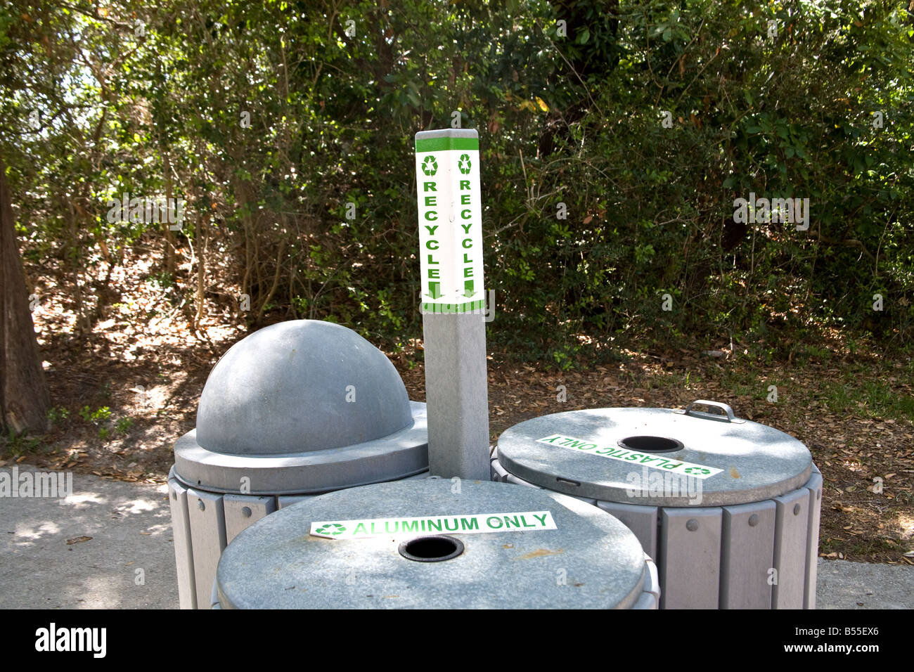 Three recycling gray trash barrels with wooden siding next to a wooded ...