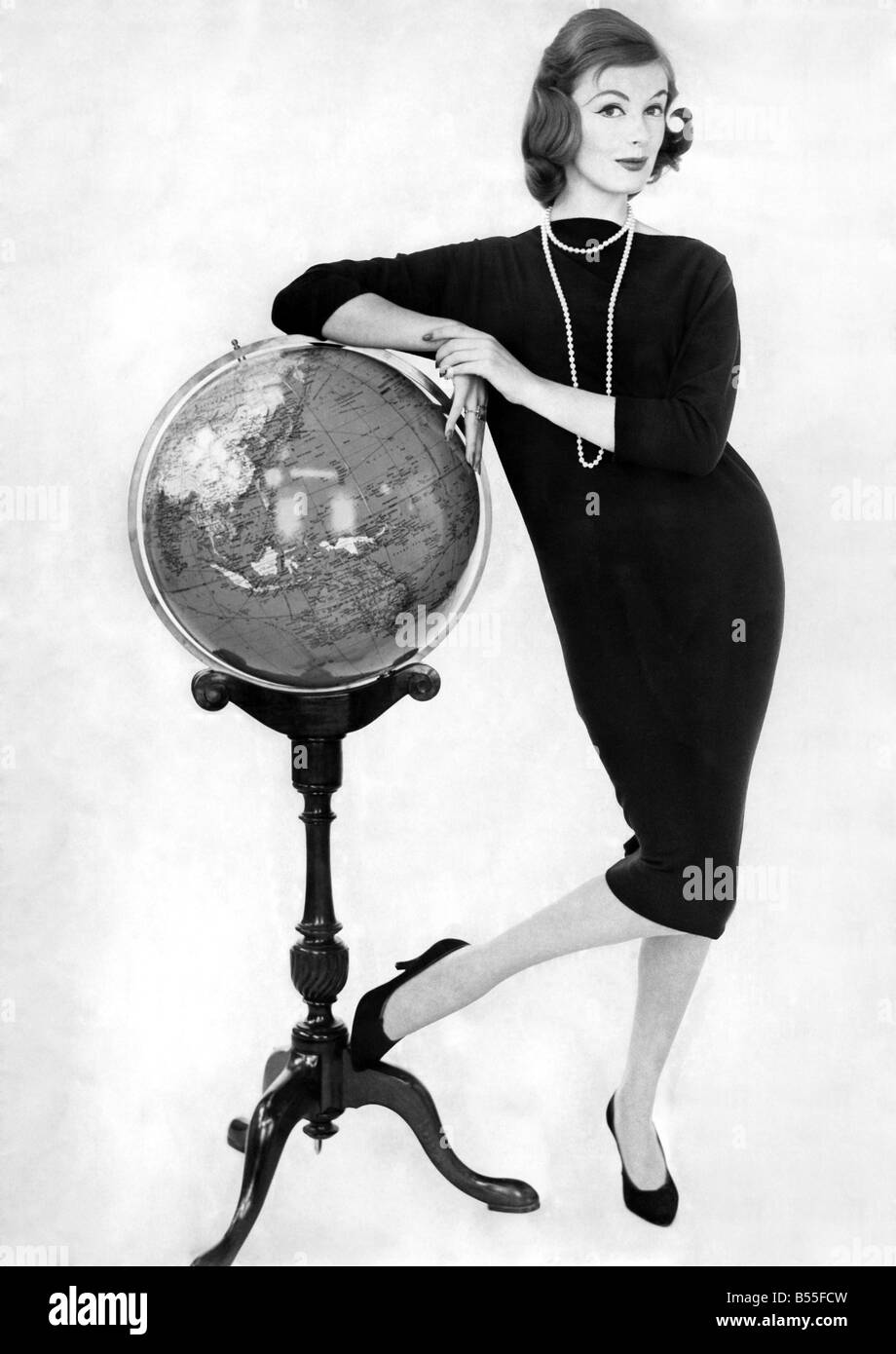 Woman wearing long dress poses leaning against a globe on a stand ...