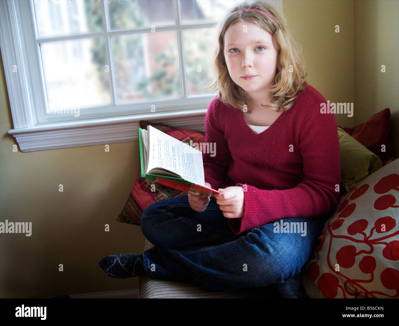 Young girl interrupts reading her chapter book on the window seat in ...