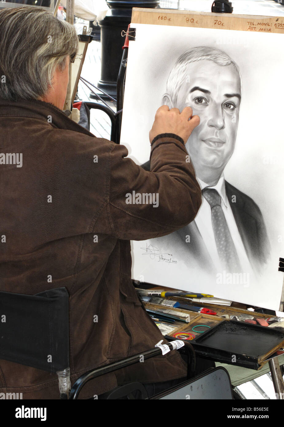 Looking over shoulder of a street portrait artist drawing at easel on ...