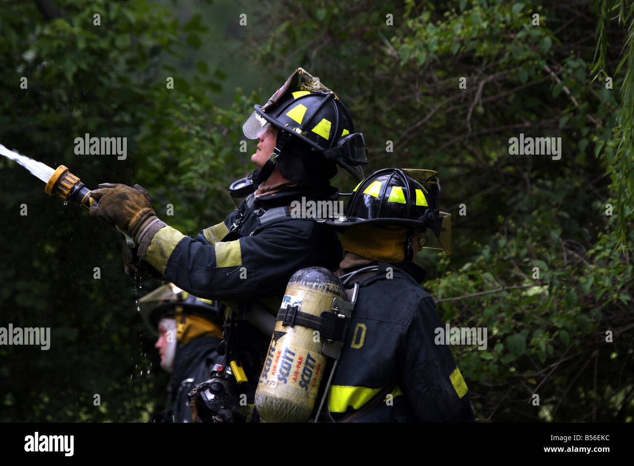 Three firefighters holding a water hose line to fight a house fire ...
