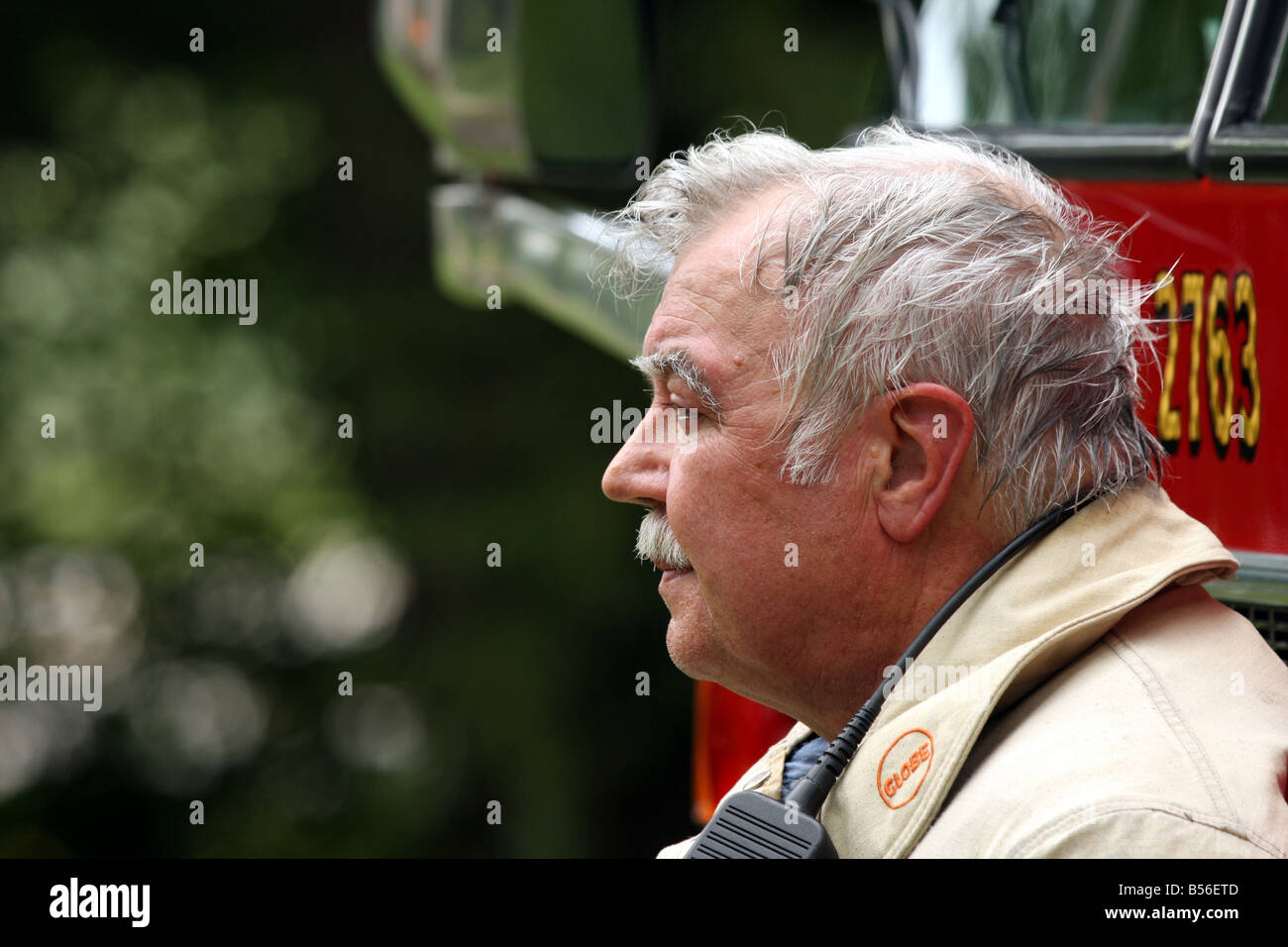 A fire chief at a scene of a hot fire resting in front of a fire truck ...