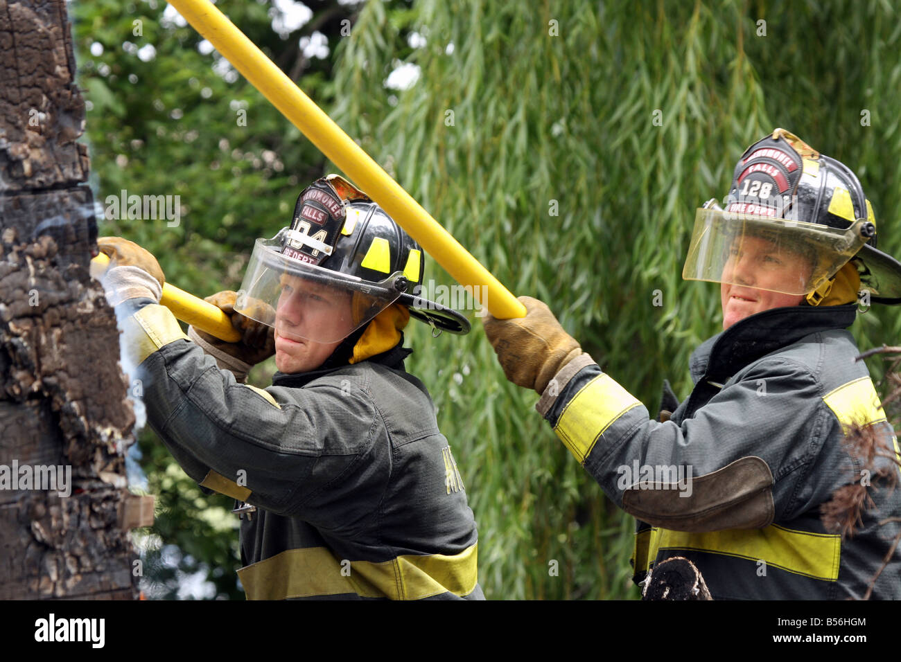 Two firefighters pushing on a burnt wall of a house that has burned ...