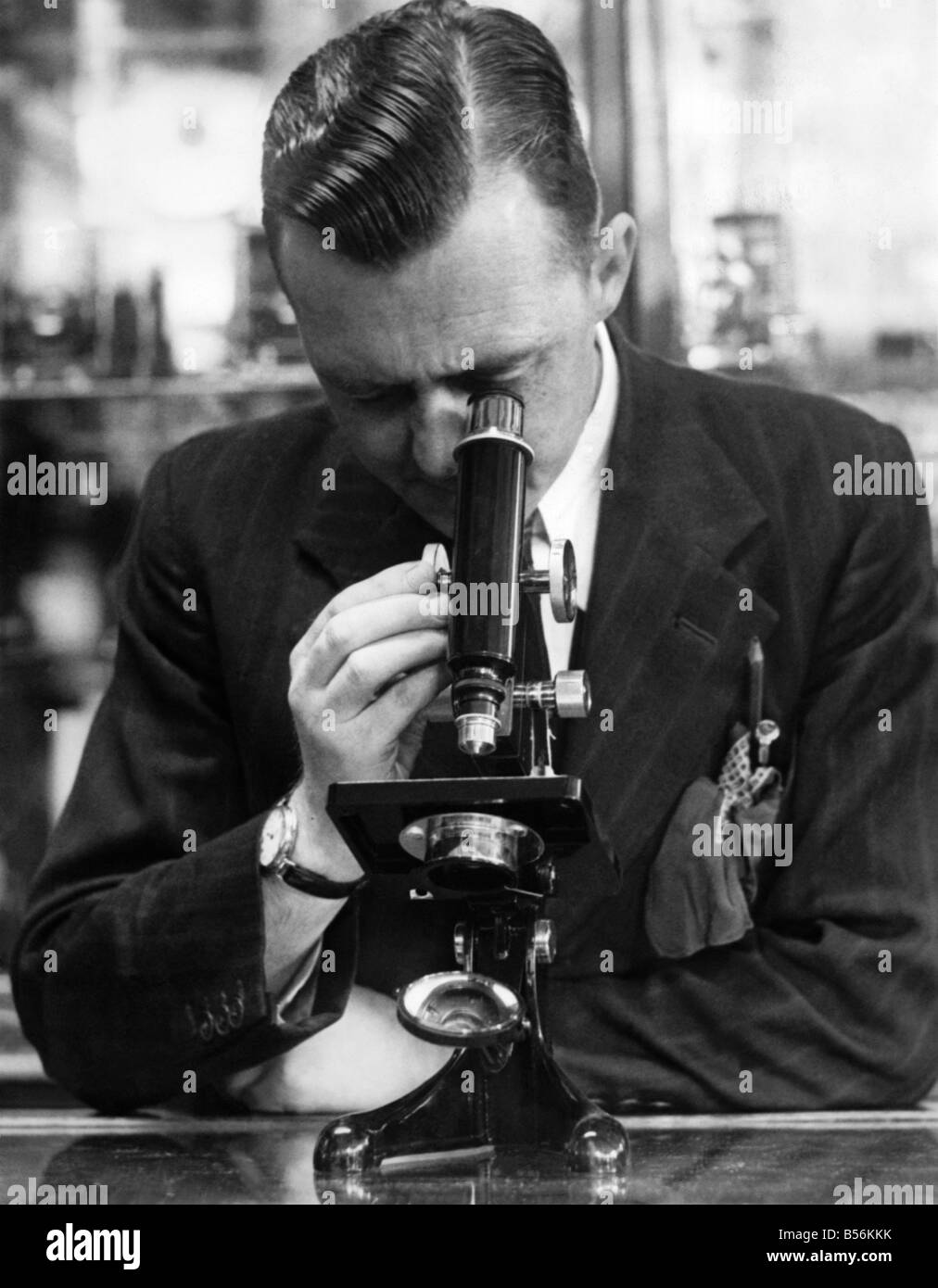A man studying a specimen under a microscope. July 1947 P009567 Stock ...