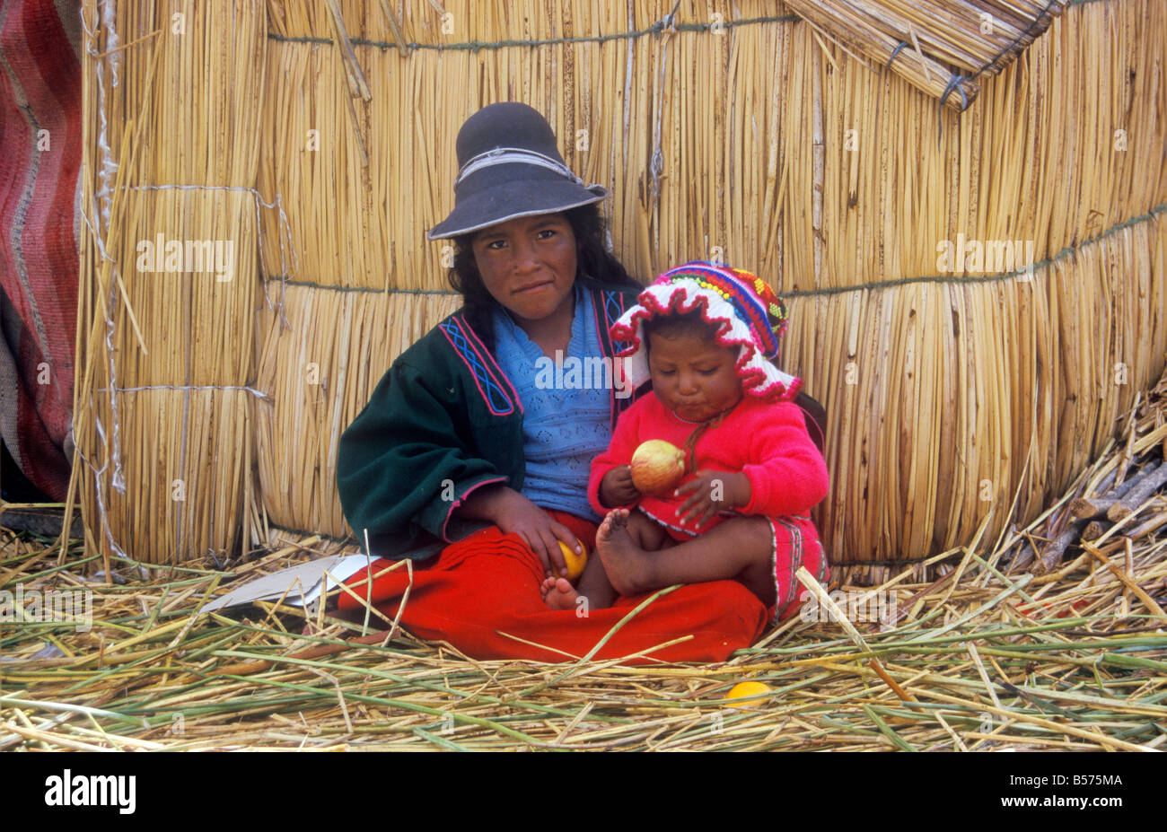 native girl and her little sister sitting beside a hut made from reed ...