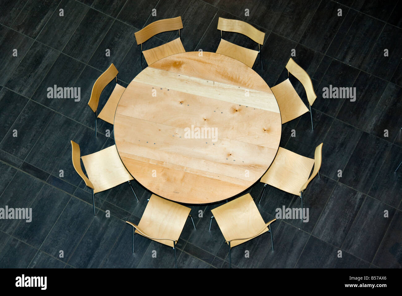 A overhead view of a wooden round table and 8 chairs on a black tiled ...
