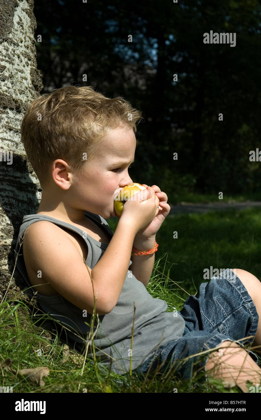 Kid eating a apple while sitting against a tree Stock Photo - Alamy