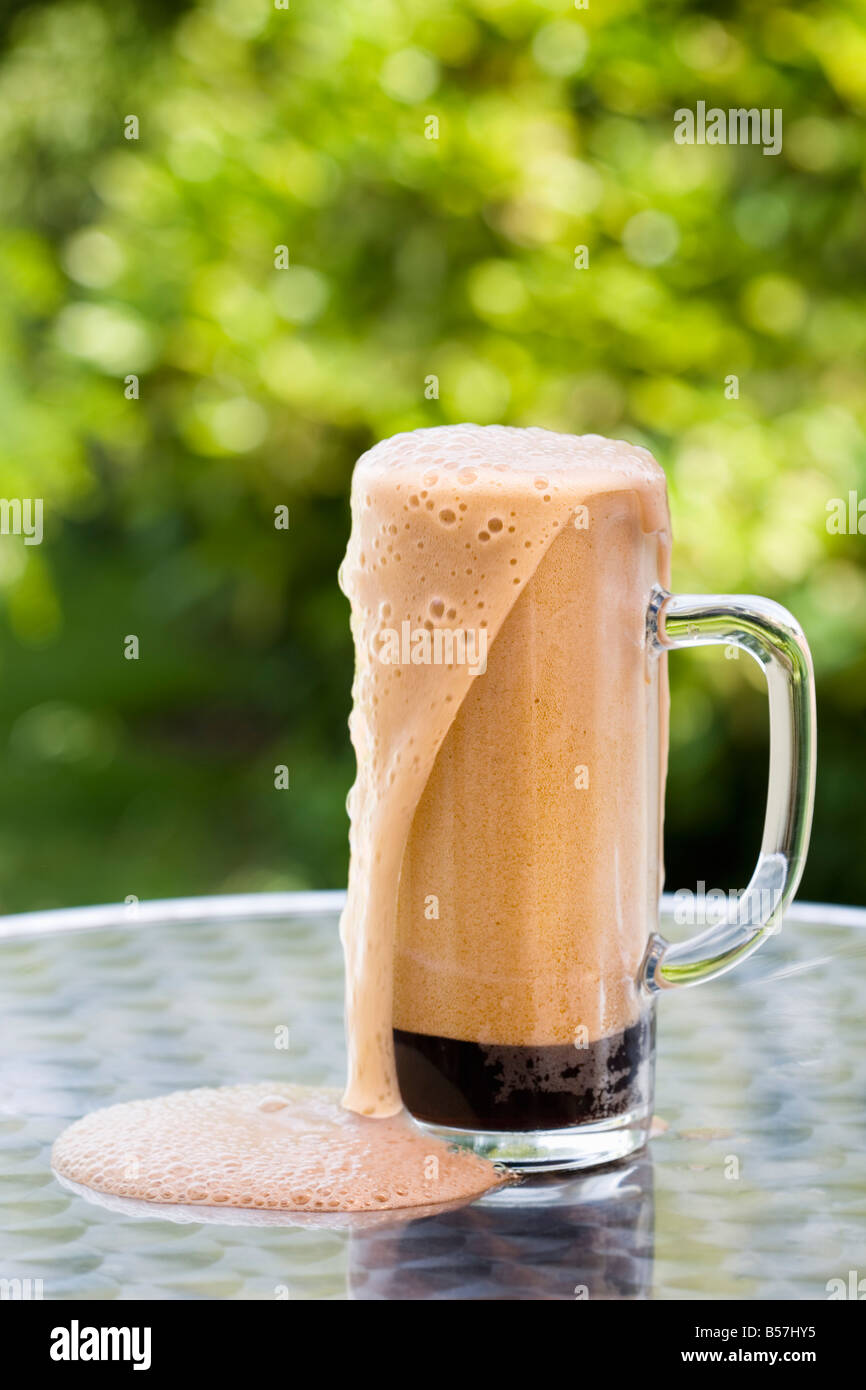 Glass of dark beer overflowing Stock Photo - Alamy