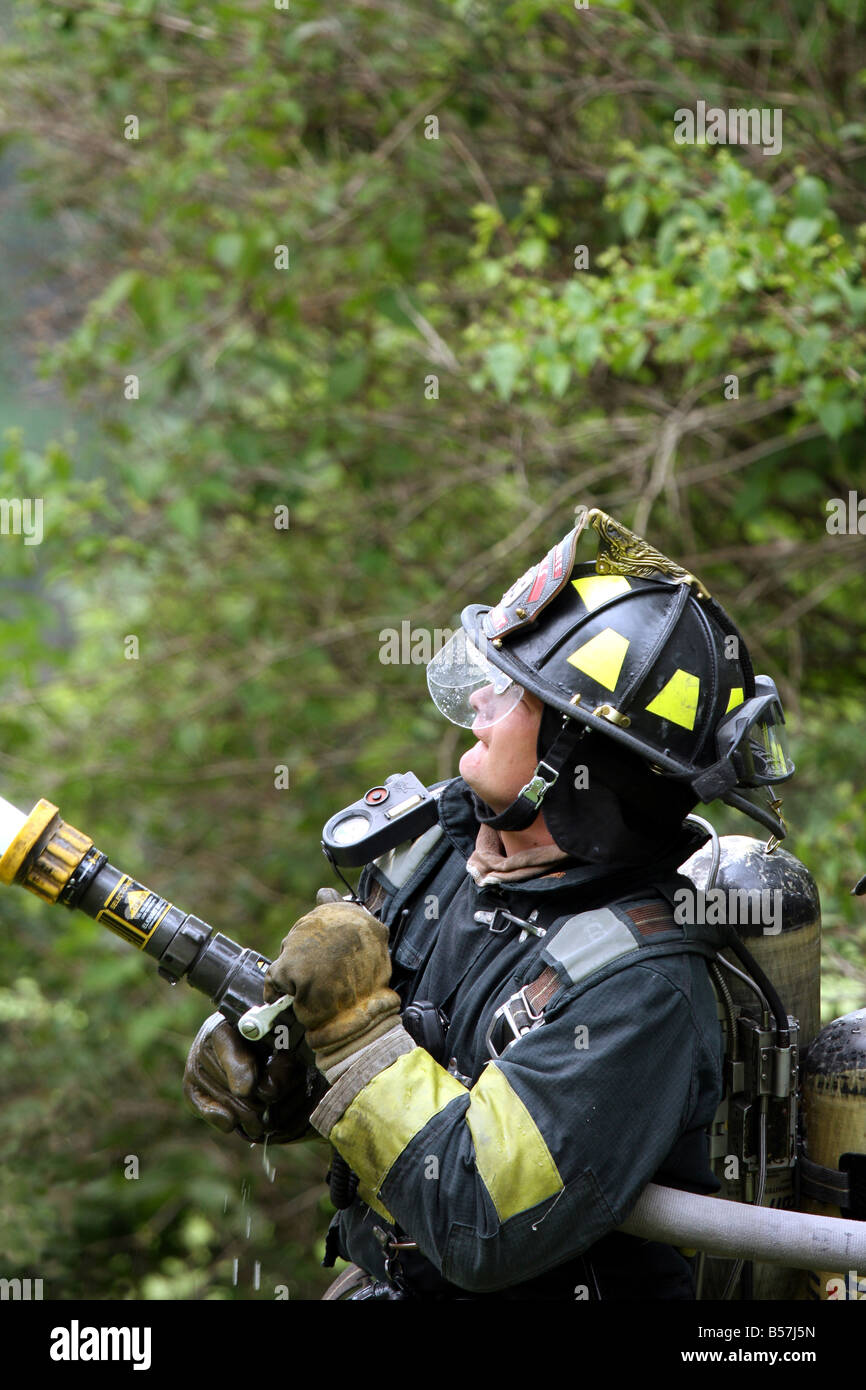 A Firefighter holding a hose line to put water on a house on fire at a ...