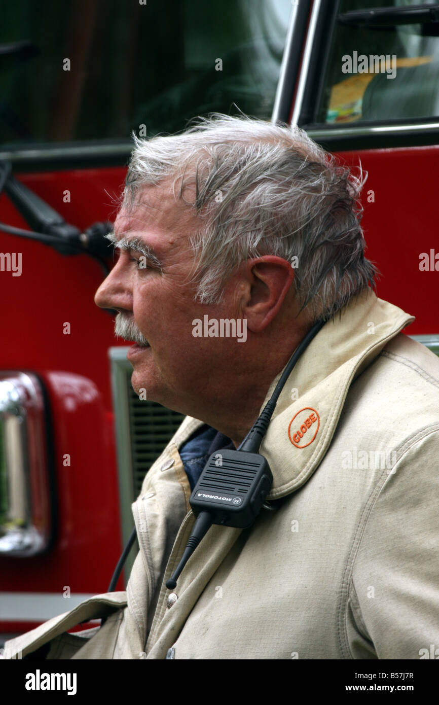 A fire chief at a scene of a hot fire resting in front of a fire truck ...