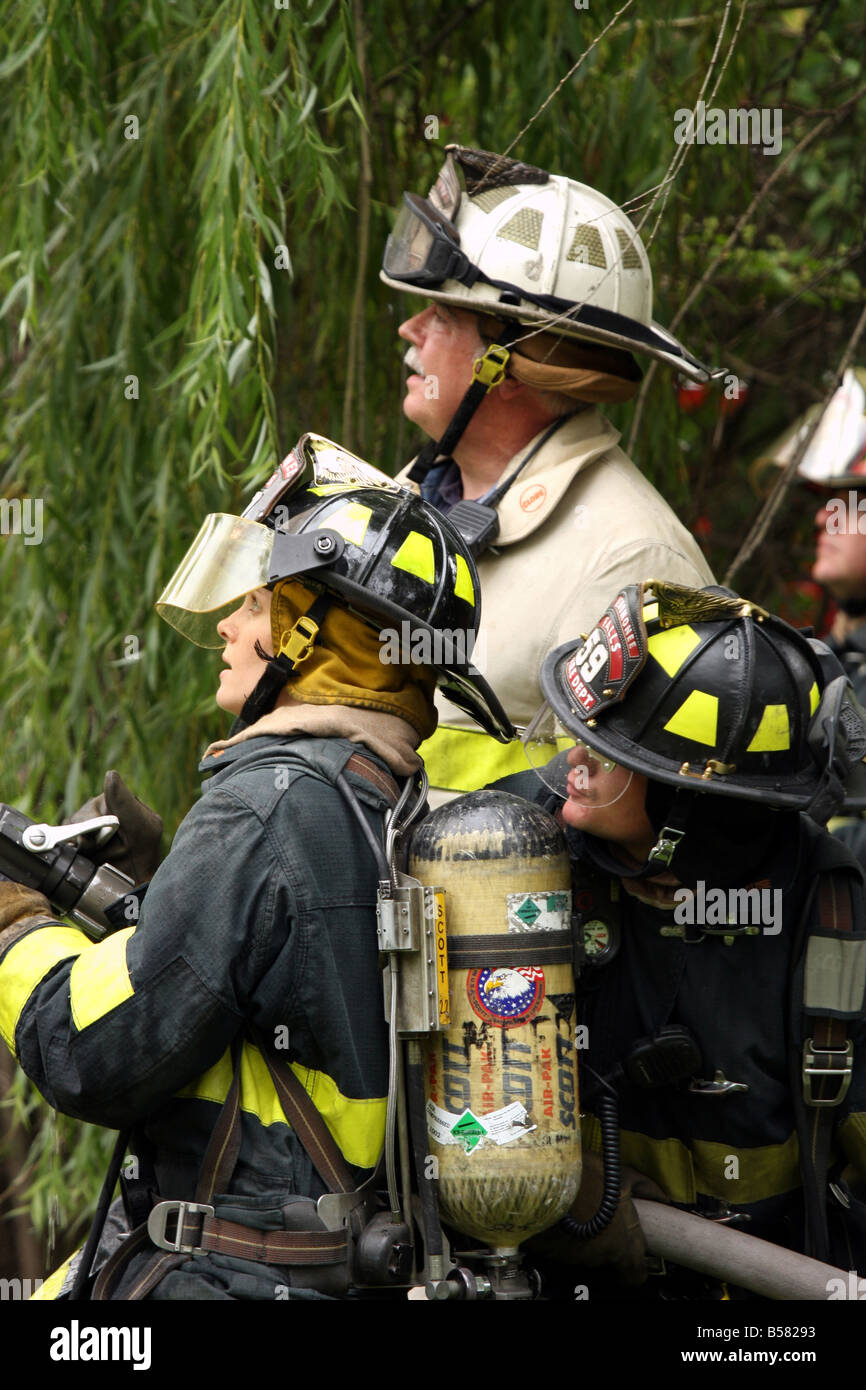 Firefighters holding a hose line to put water on a house on fire at a ...