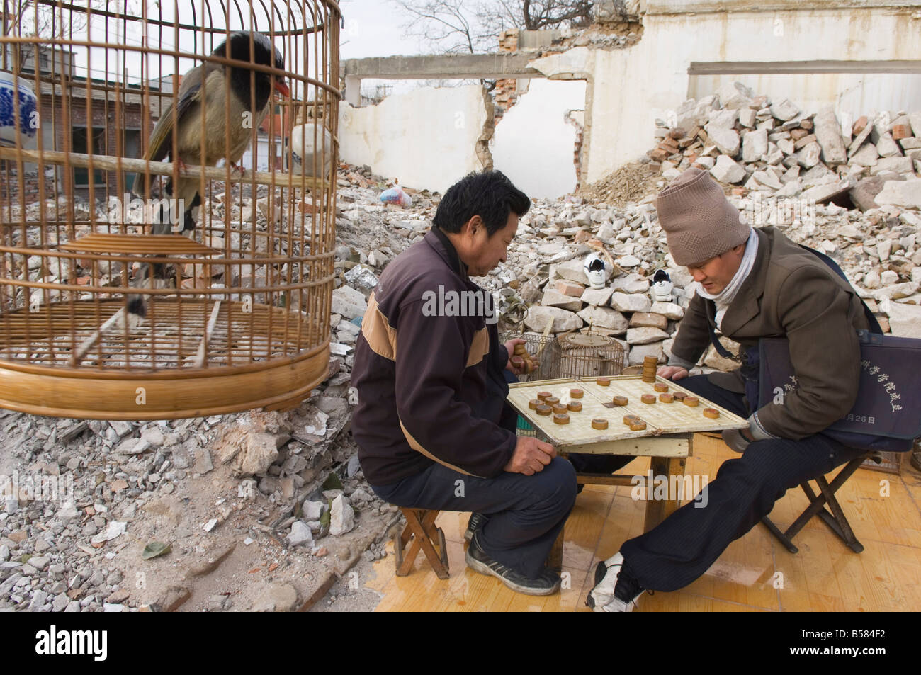 Men playing a board game in a neighbourhood Hutong partially destroyed and marked for demolition ...