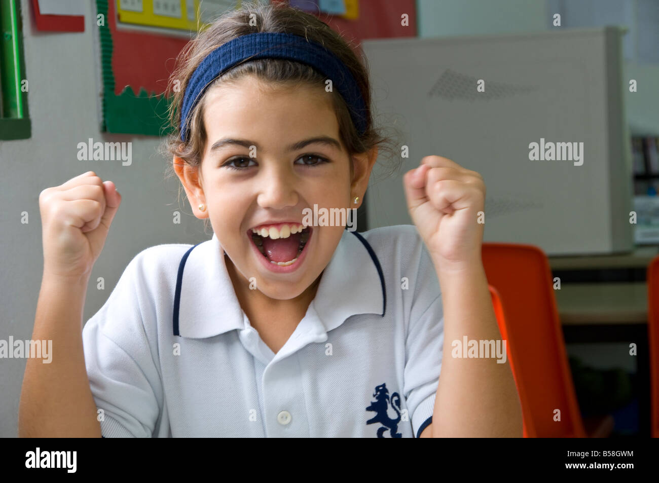 Junior schoolgirl happy and excited at her desk in school classroom ...