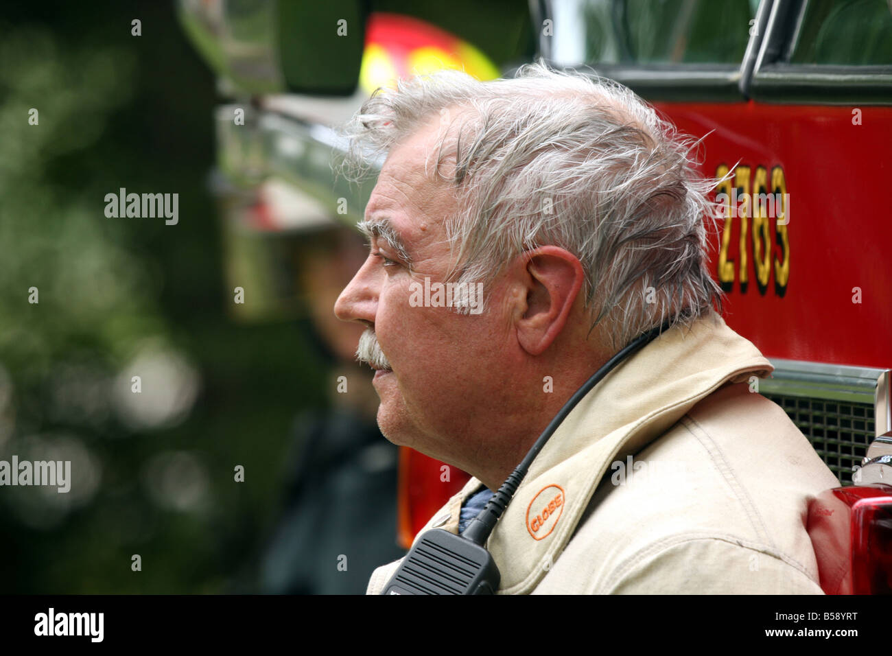 A fire chief at a scene of a hot fire resting in front of a fire truck ...