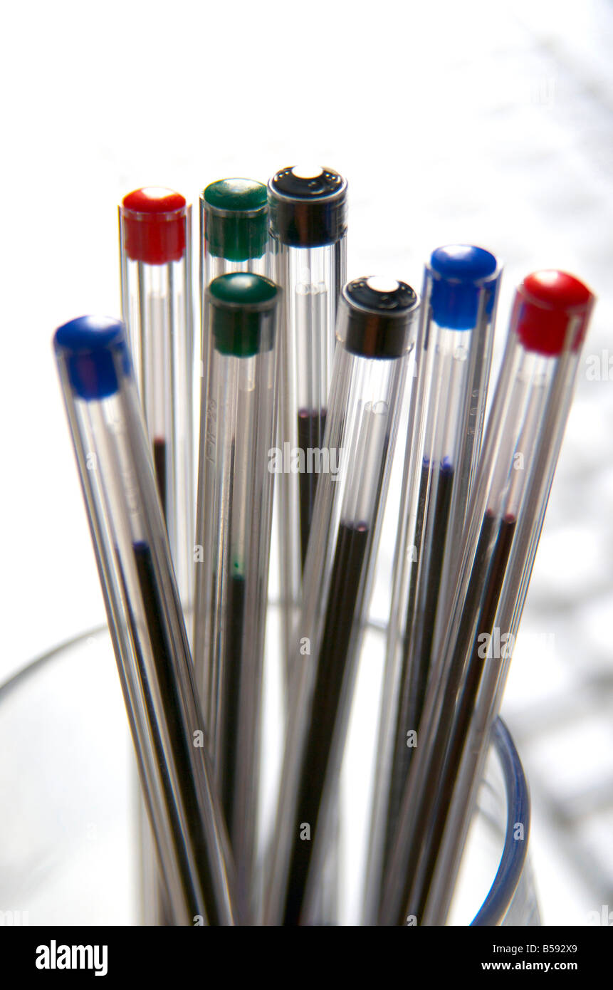 Colorful pens arranged vertically in a clear glass container against a ...
