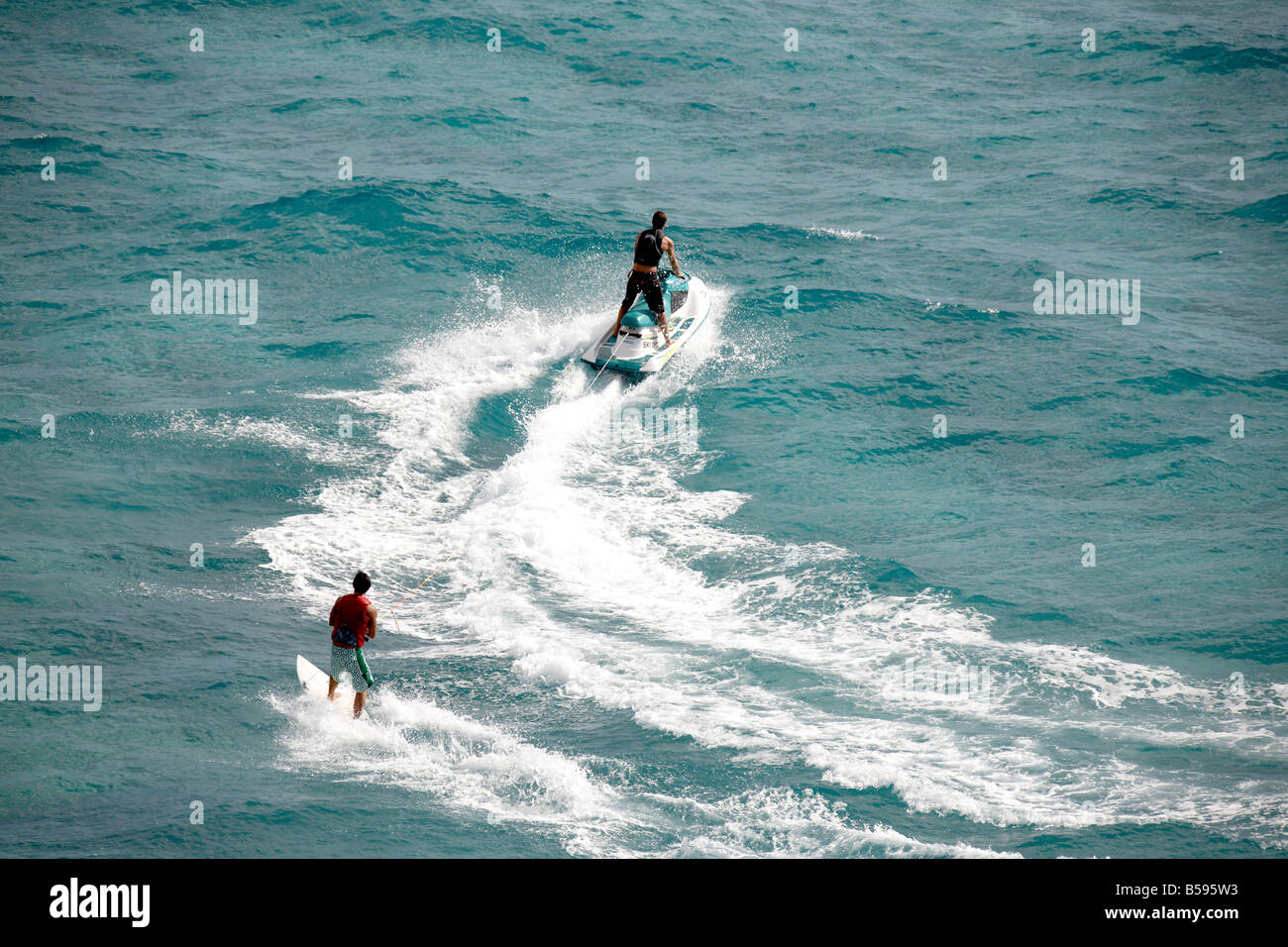 Waterskier on surf board water skiing being towed by man on jet ski in ...