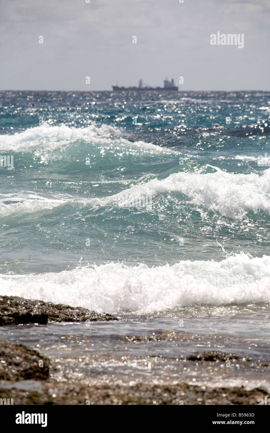 Crashing waves on rocks with out of focus merchant ship on sea in ...