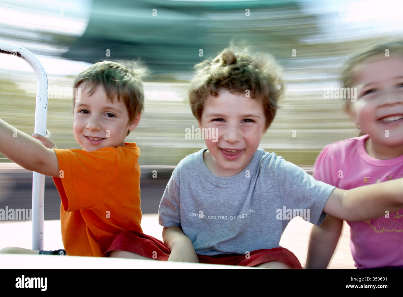 Three children having fun on a playground merry go round in a park in ...