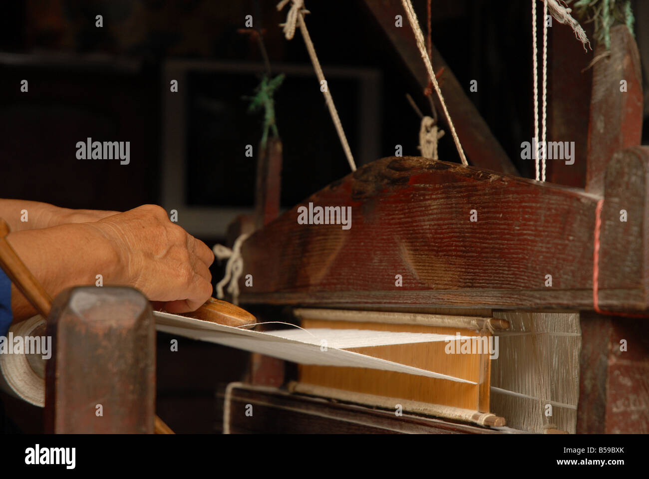 A woman works a loom, crafting traditional clothing in a traditional ...