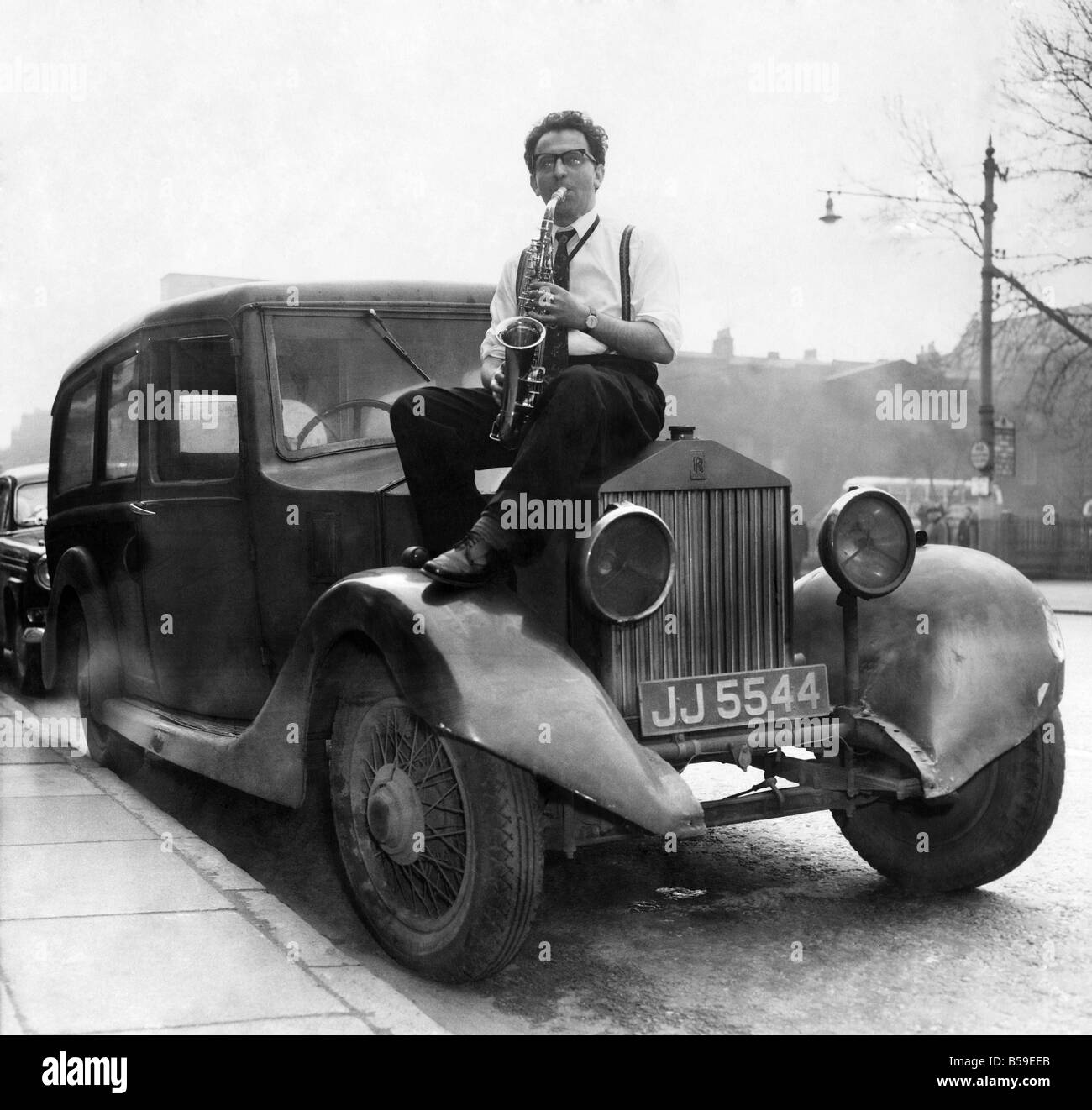 Musician Johnny Roadhouse sitting on the bonnet of a car playing his ...
