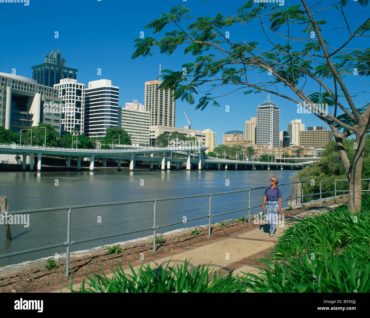 A tourist walking beside the Brisbane River with the city skyline ...