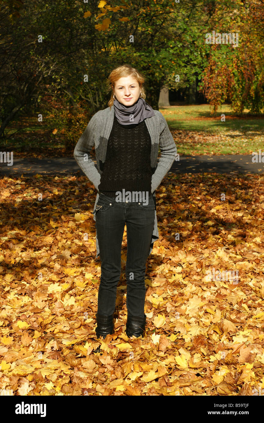 Young student standing in the middle of golden leaves under a tree ...