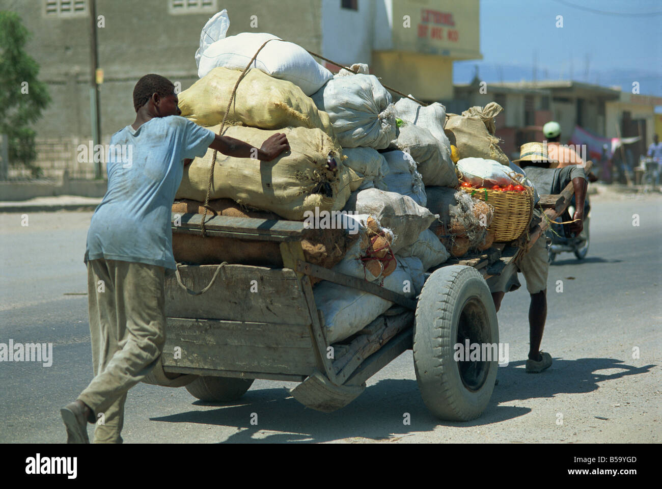 Men pushing and pulling heavily loaded cart along road Port au Prince ...