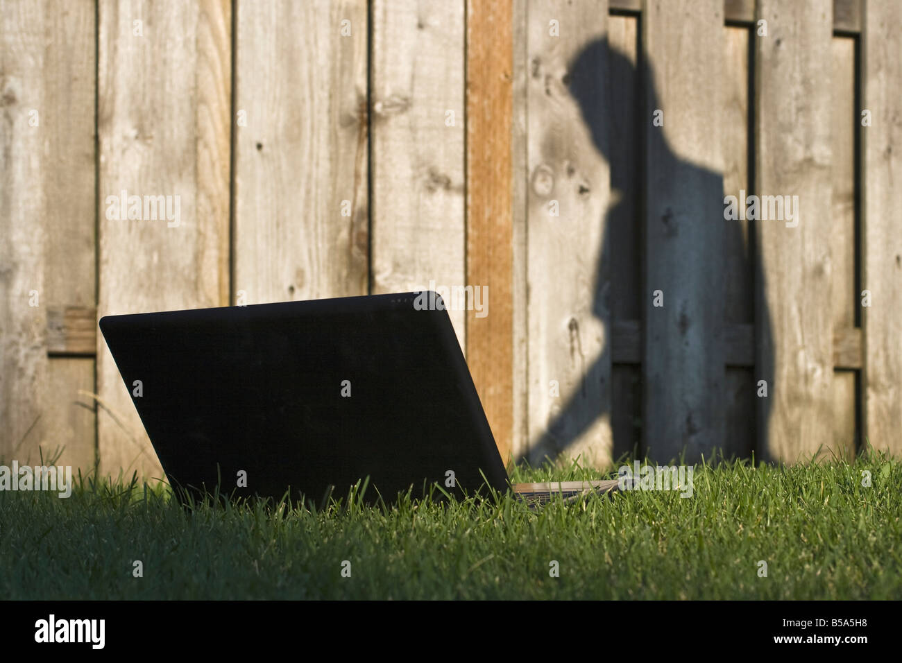 Man's shadow on a fence looks like it is using a computer lying in the ...