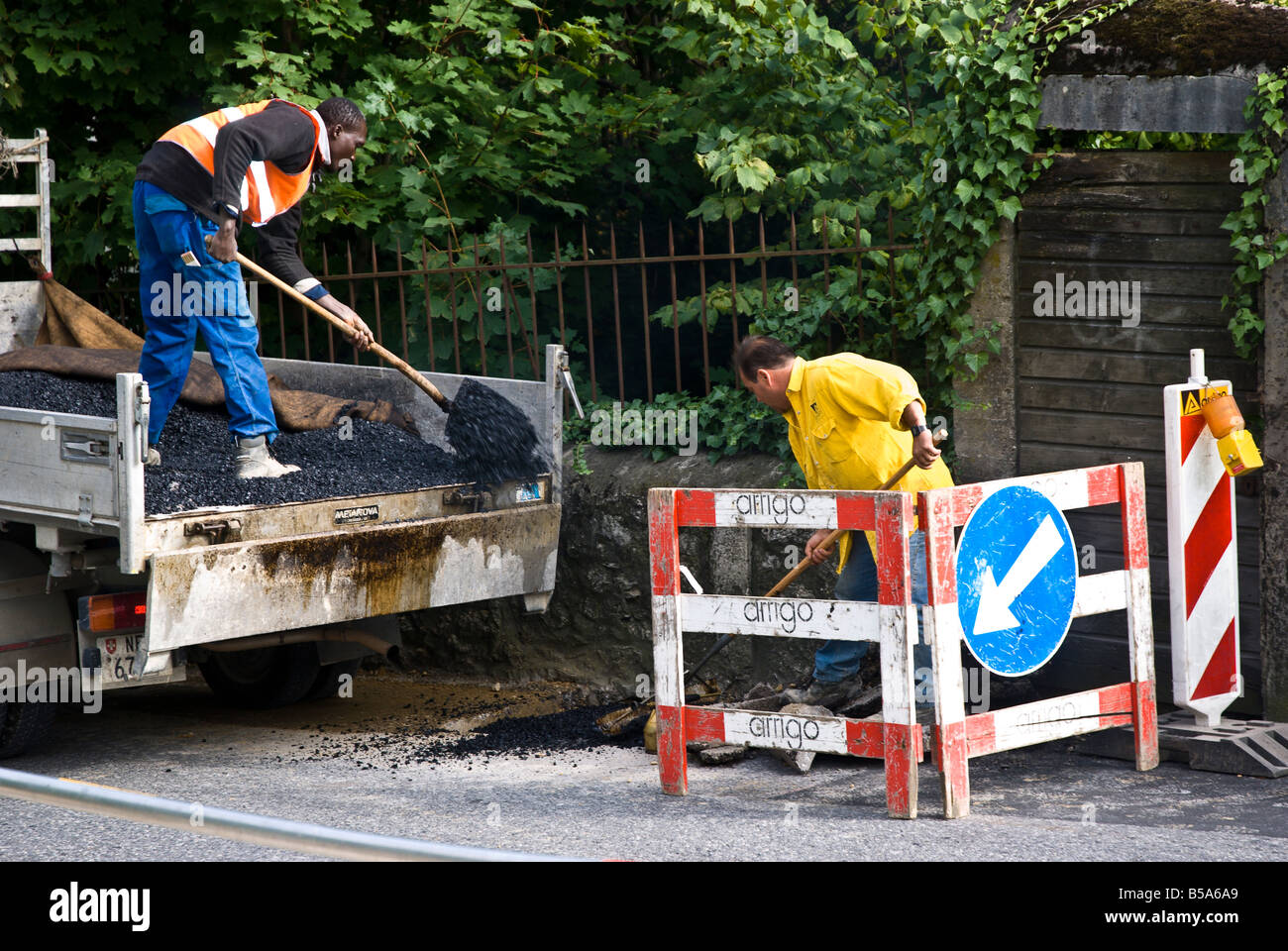 Two construction workers work on fixing holes in the road Stock Photo ...