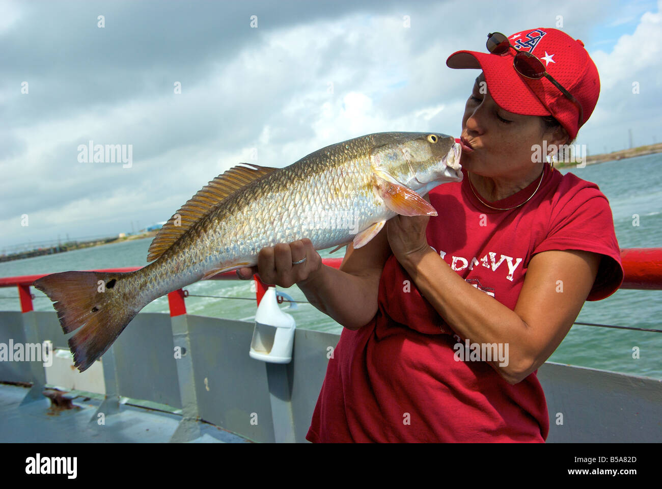 Woman angler holding and kissing red fish on group fishing party boat ...